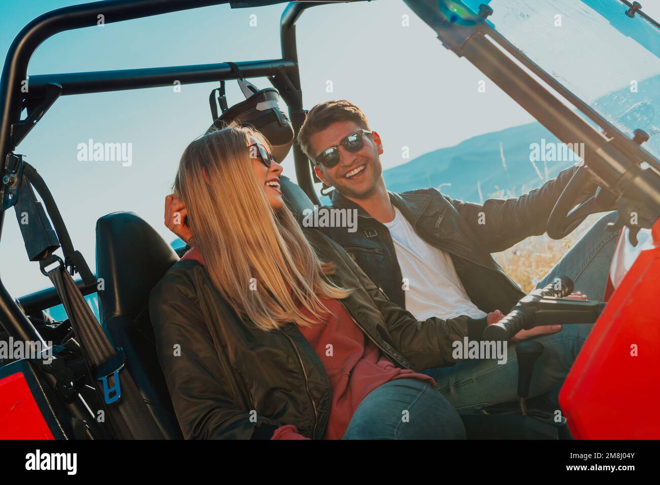 Young happy excited couple enjoying beautiful sunny day while driving a off road buggy car on ...
