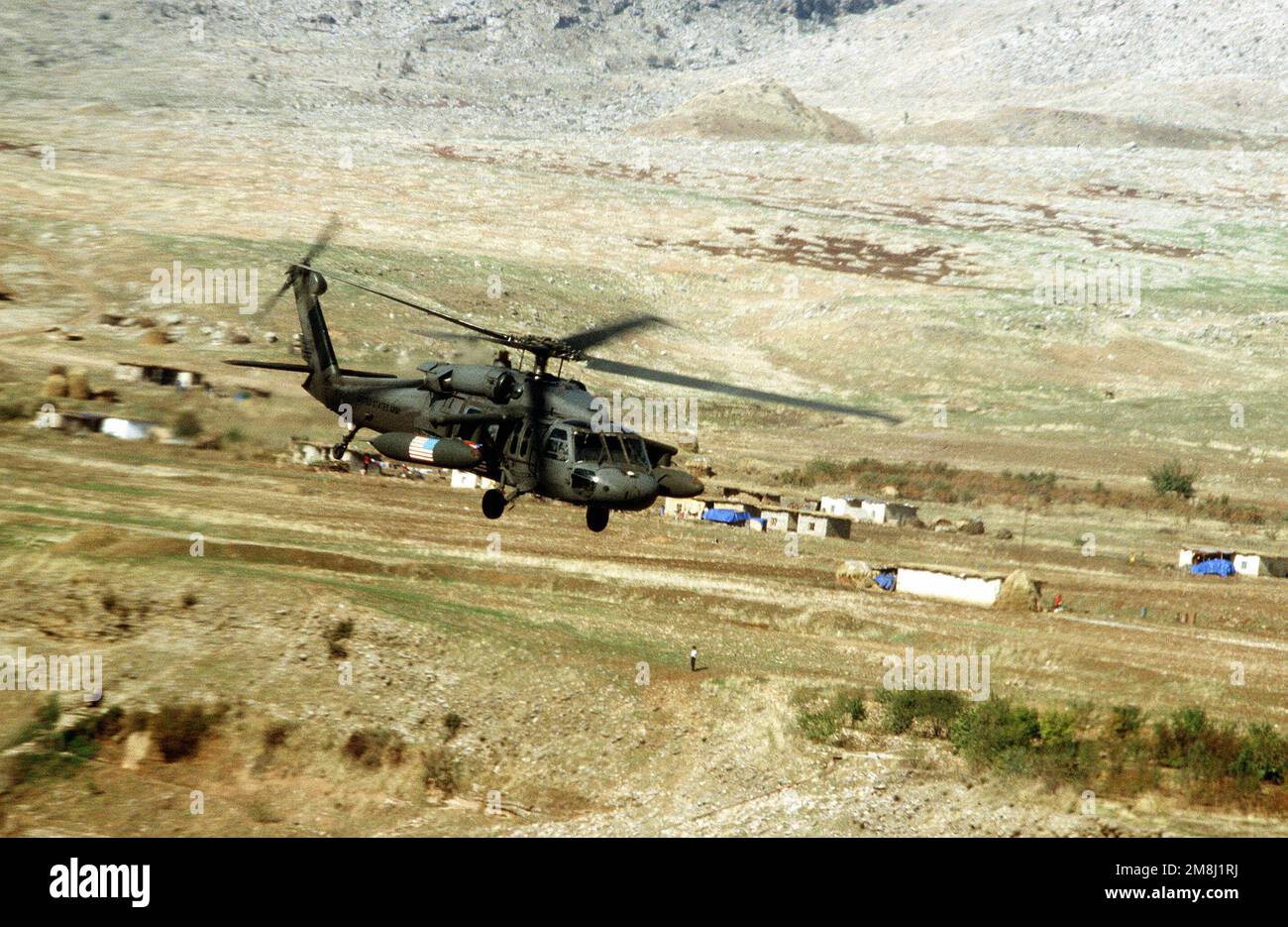 A UH-60A Black Hawk (Blackhawk) helicopter flies over a small village ...
