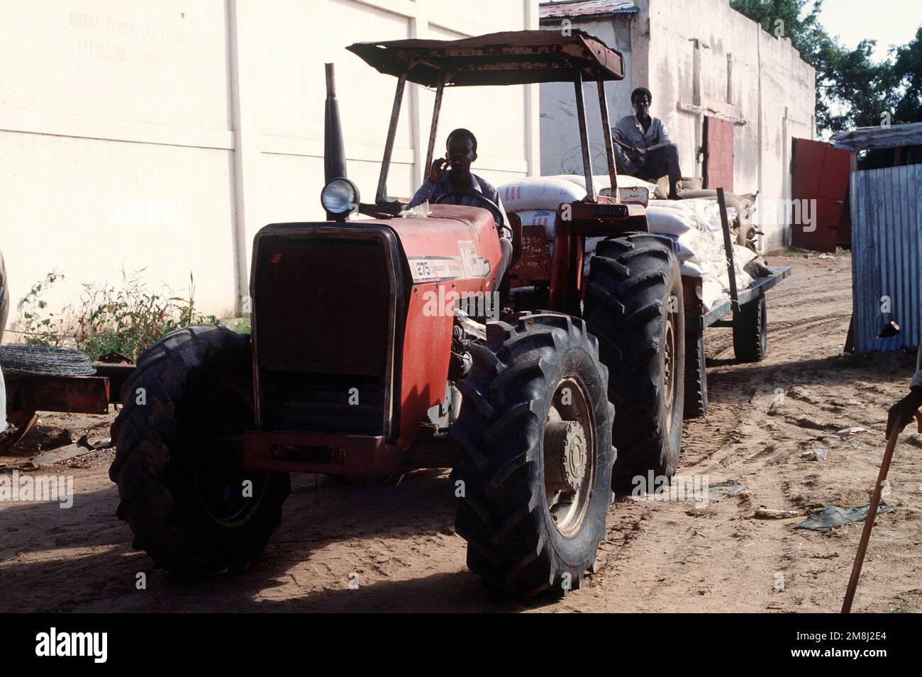 A Somali man drives a tractor pulling a trailer full of supplies at the ...
