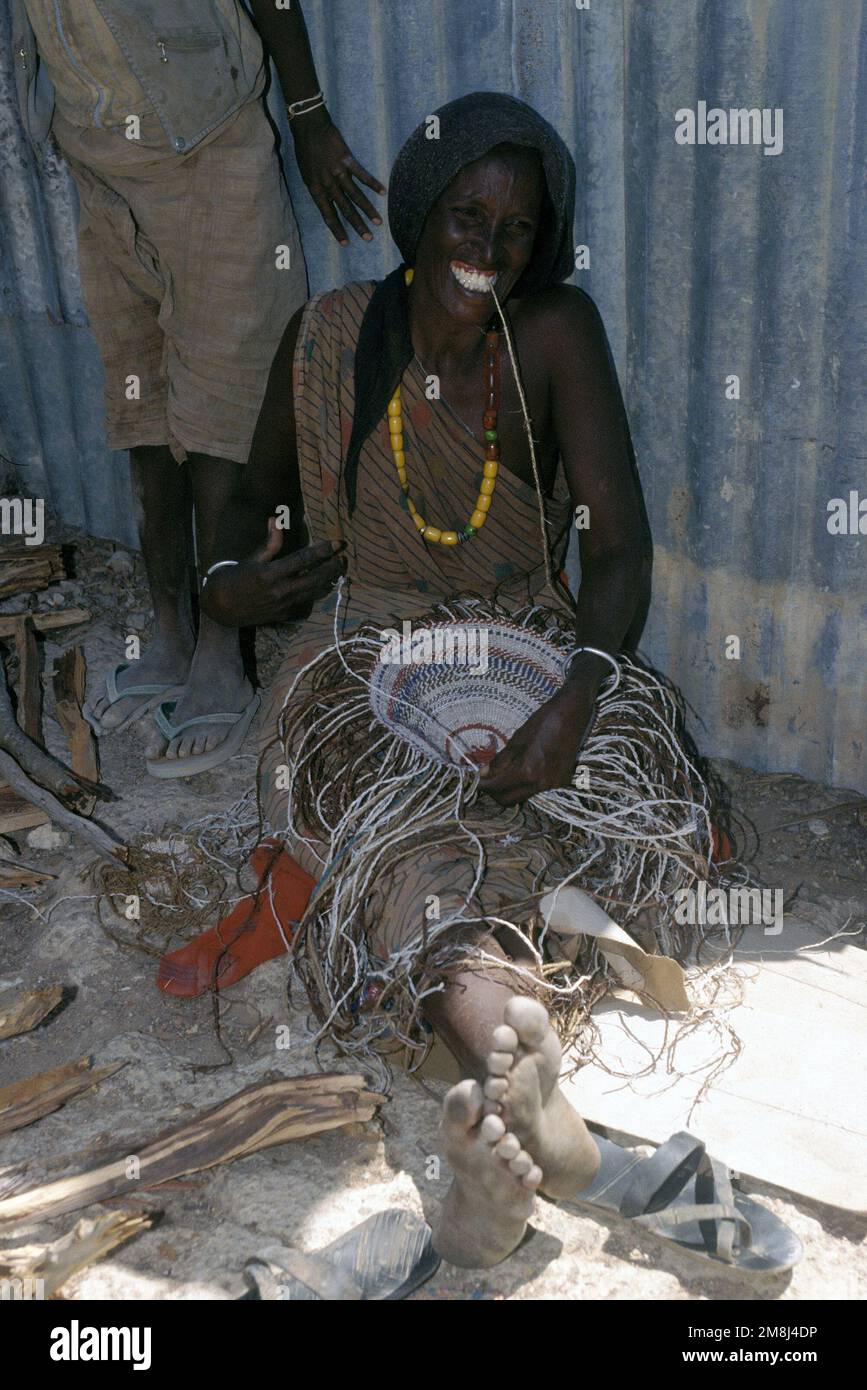 A Somali woman laughs as she does basket weaving on the street. Subject ...