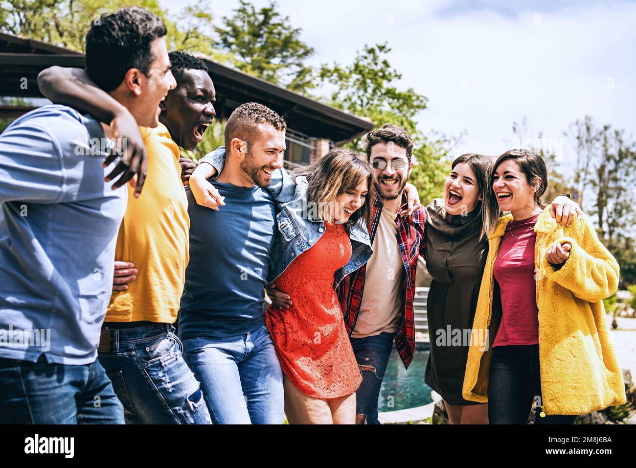 Seven friends, diverse in ethnicity, laugh and stand united in a park ...