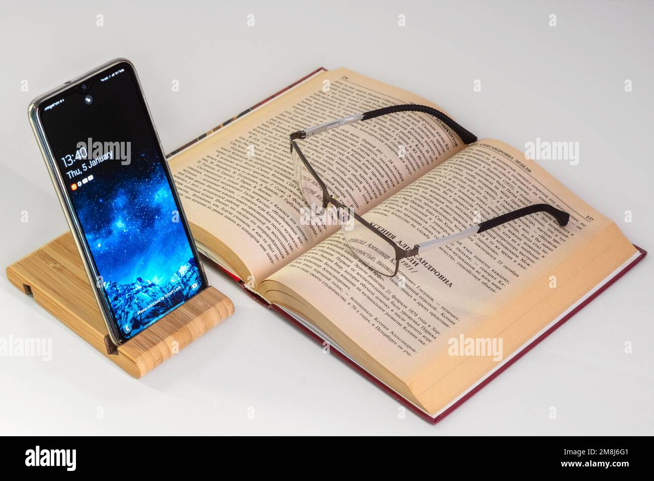 Switched on mobile phone installed on a special stand and an open book ...