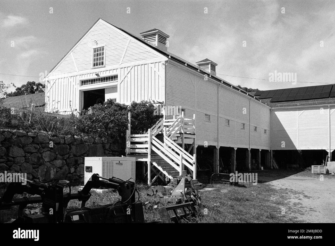 Farm equipment sits on the ground below a large white barn containing ...