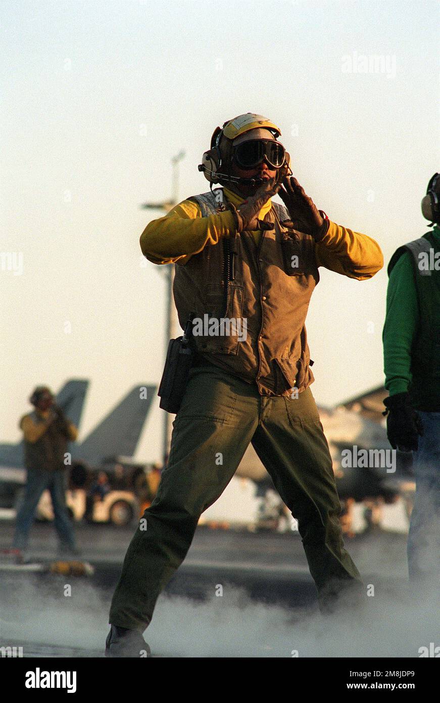A plane captain signals an aircraft to move forward on the catapult ...