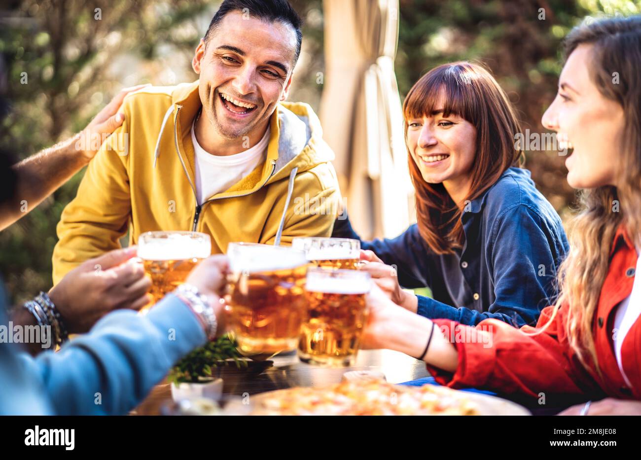 Young friends drinking and toasting beer pints at brewery bar garden ...