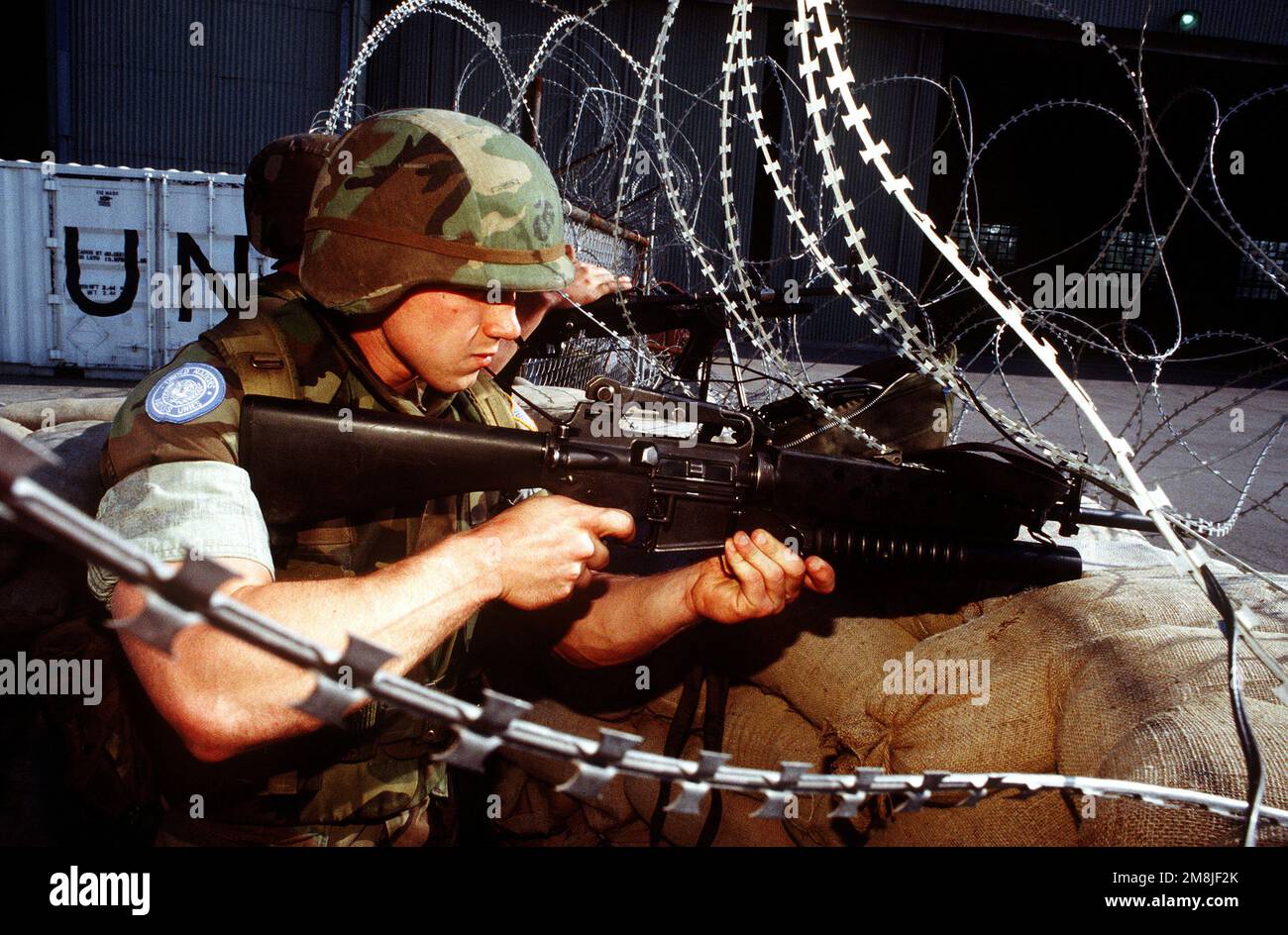 Protected by concertina wire, a US Marine stands ready as he aims his M ...