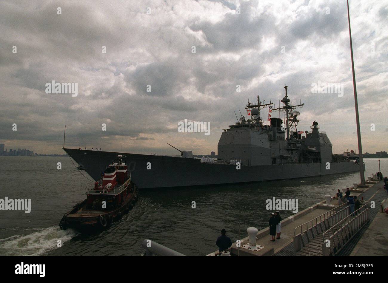 A civilian tugboat helps push the guided missile cruiser USS NORMANDY ...