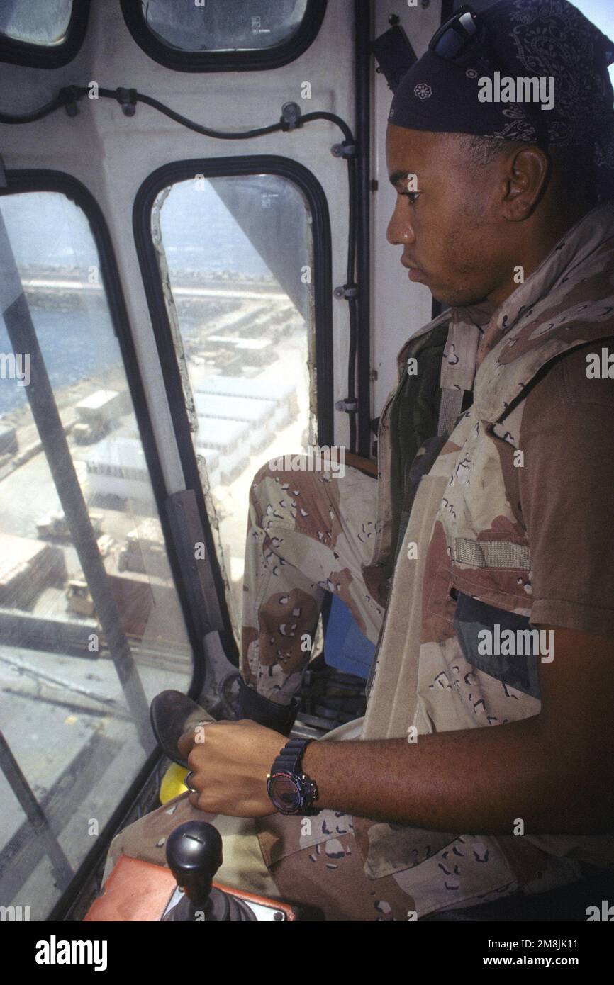 A crane operator onboard the USNS Denebola loads vehicles from the pier ...