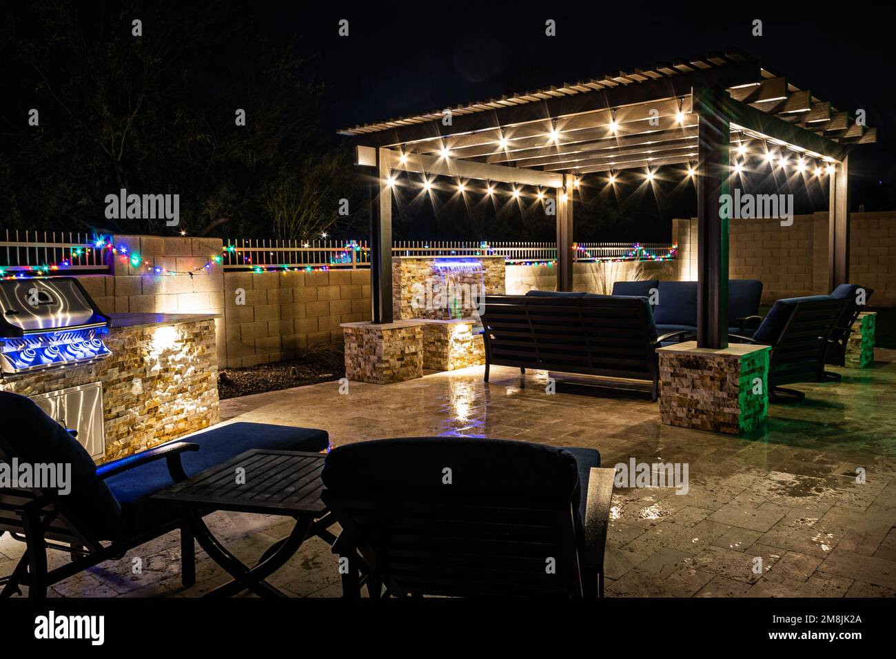 A resort style backyard at night with a waterfall, pergola, and a firepit at night Stock Photo ...