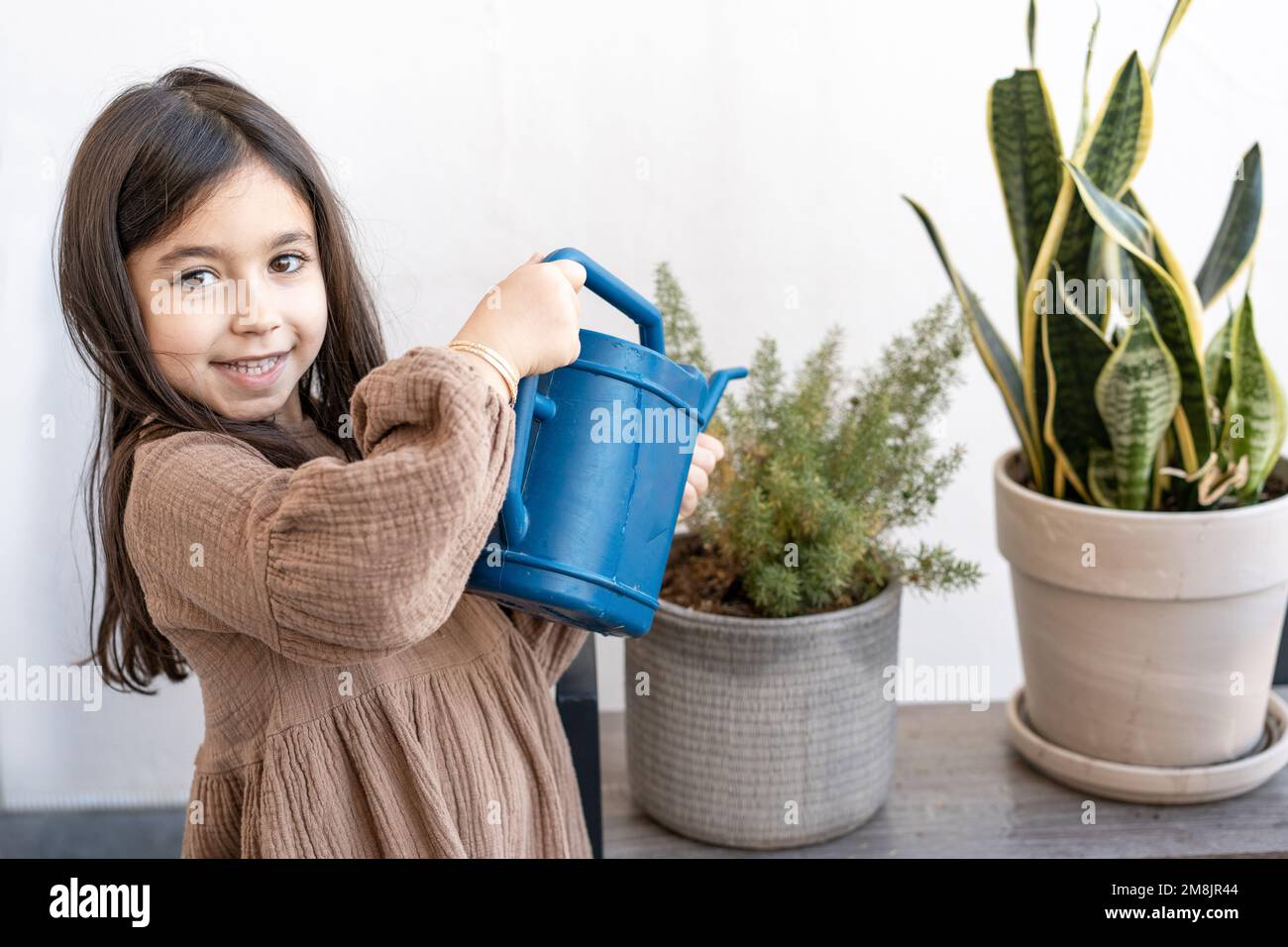 Little girl is watering plants with water can on roof terrace. Active ...