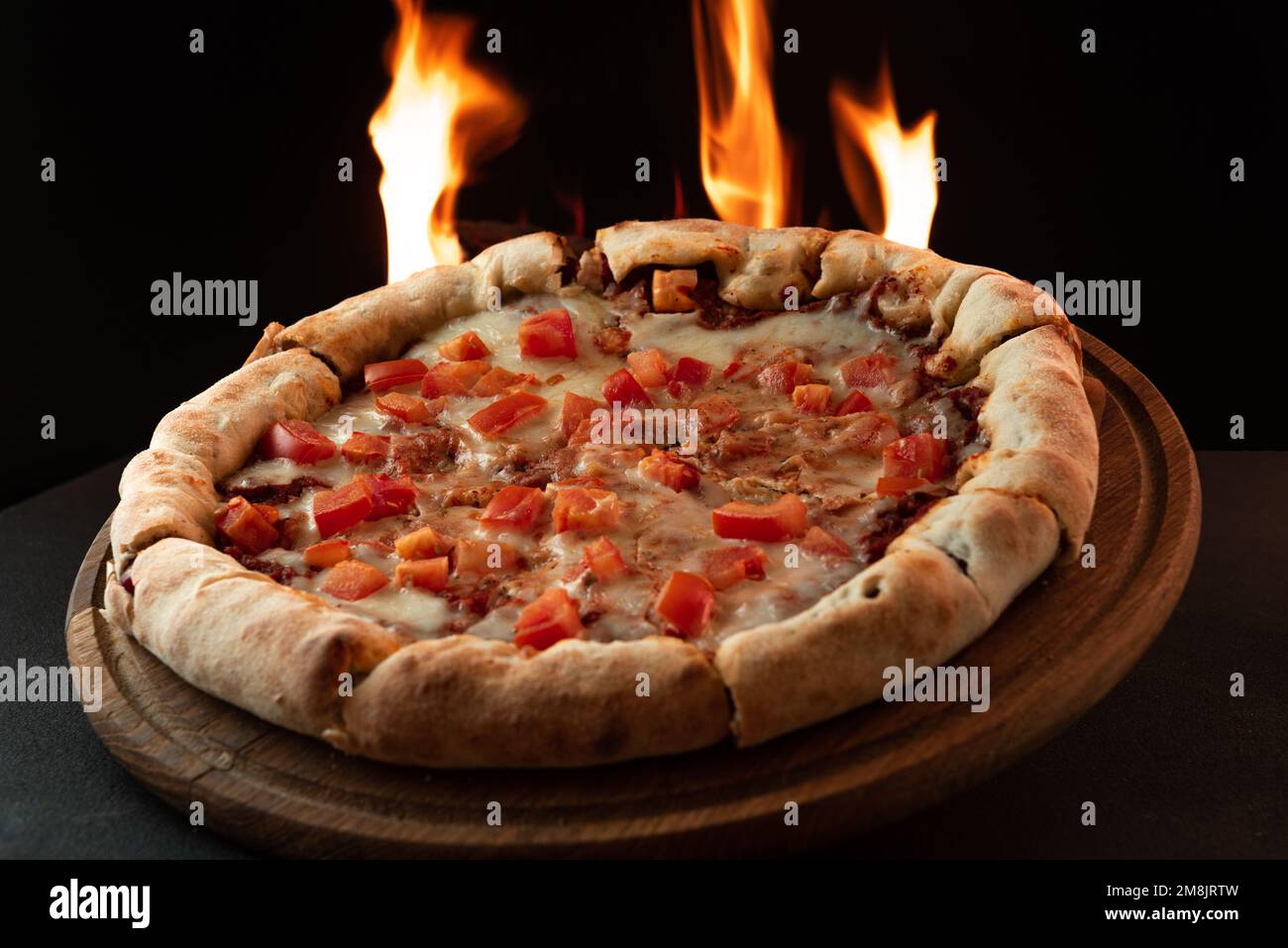 Neapalitan pizza with tomatoes on dark background with fire. Cooking ...