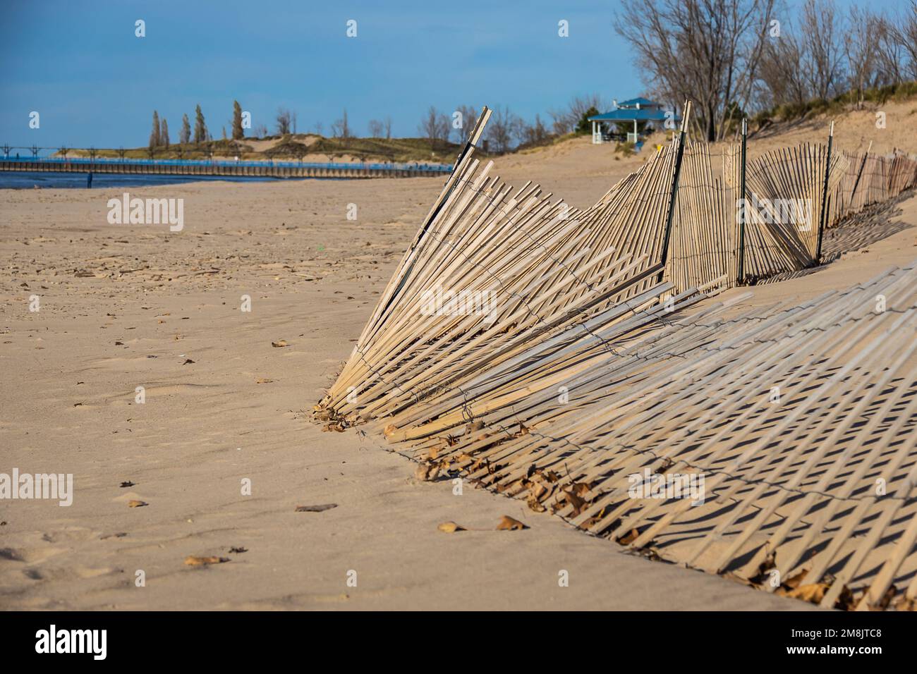 A fence in a sand dune with many diagonal lines and sunlight casting ...