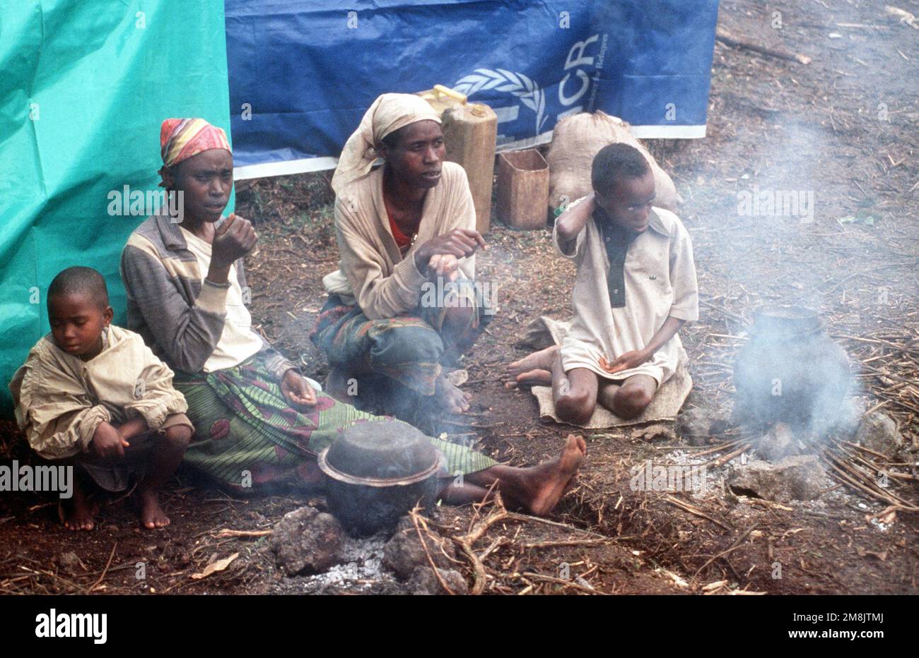 A refugee family sits near a smoldering fire in the camp near Goma ...