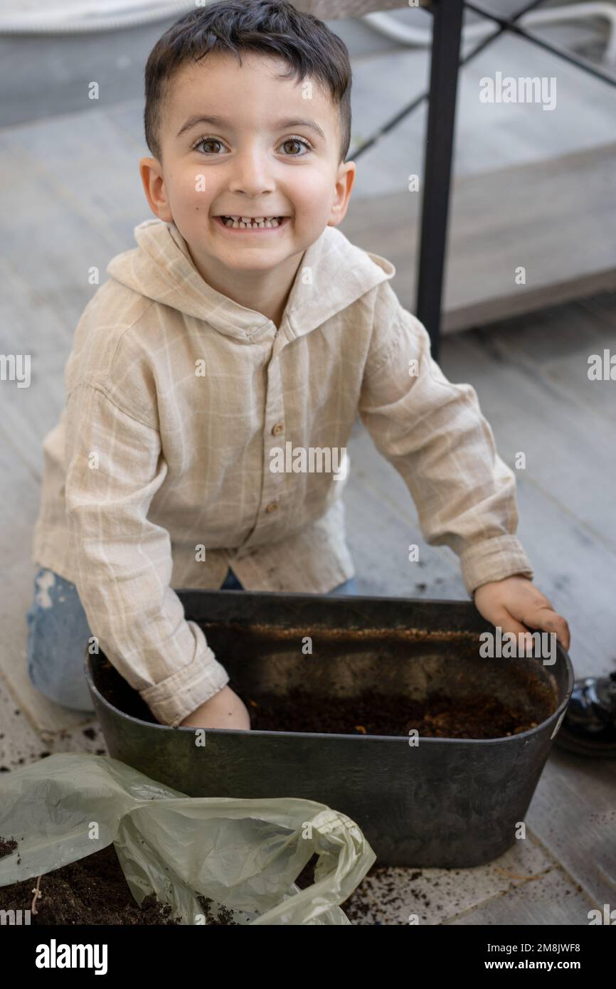 Funny boy planting in home. Little child shovels ground, putting soil ...