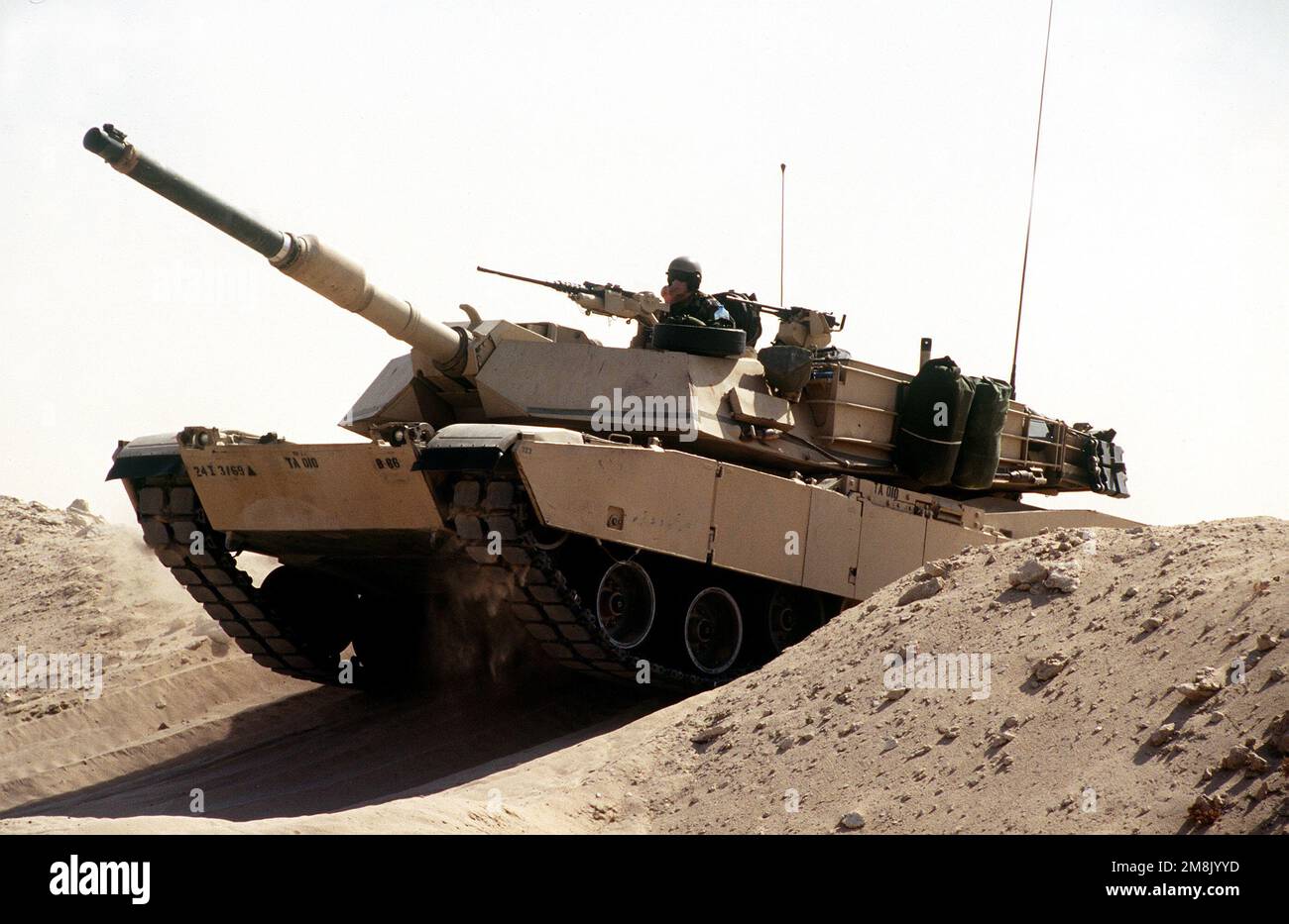A M1A1 Abrams tank breaches a berm in the desert during maneuvers ...