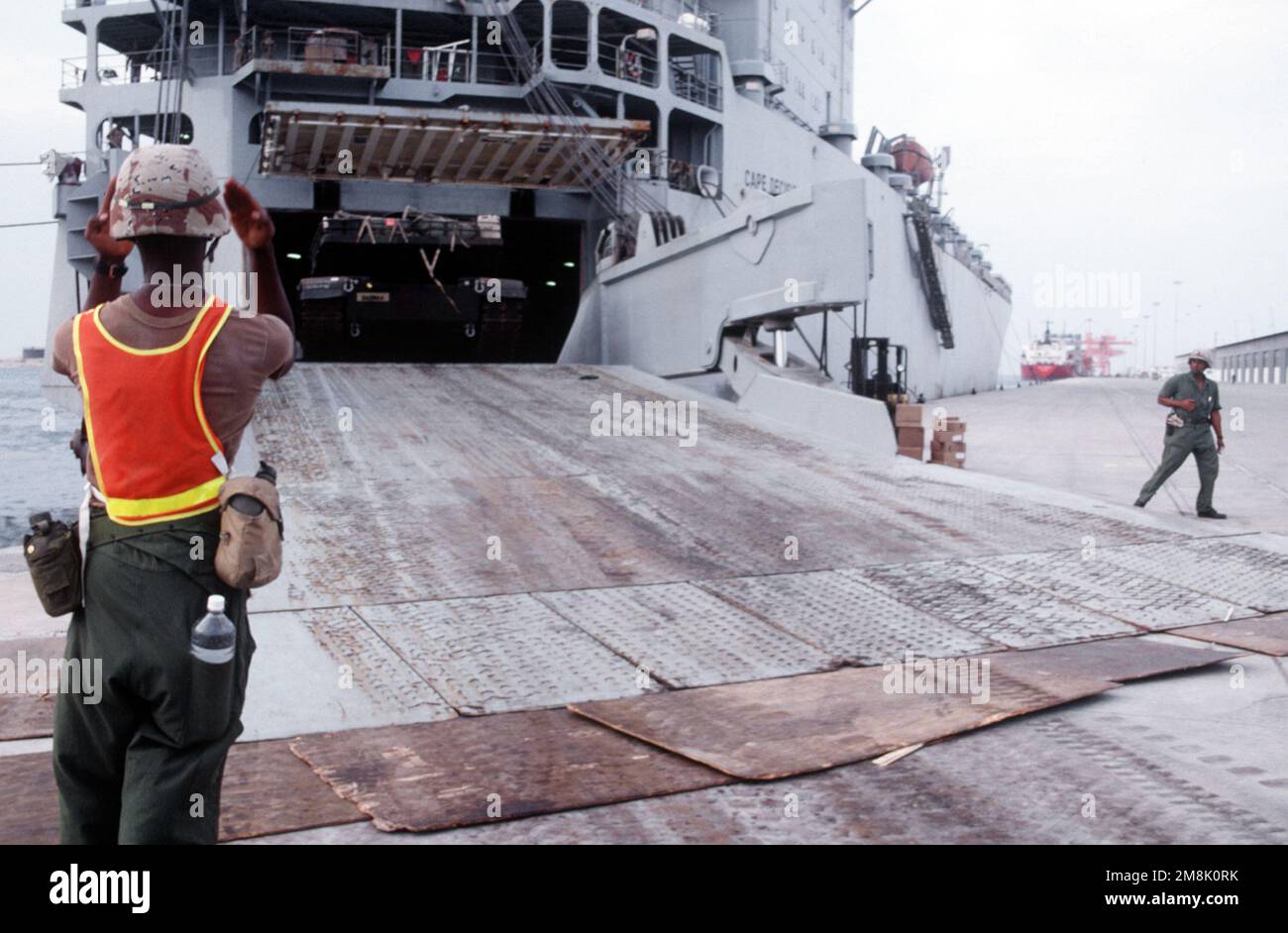 A US Army stevedore directs a M-1 Abrams Main Battle Tank down the ramp ...