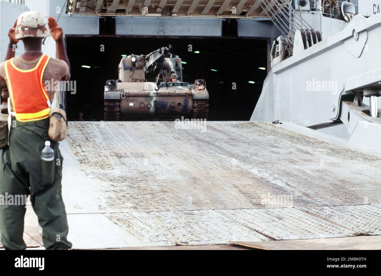 A US Army stevedore directs a M88A1 recovery vehicle down the ramp of ...