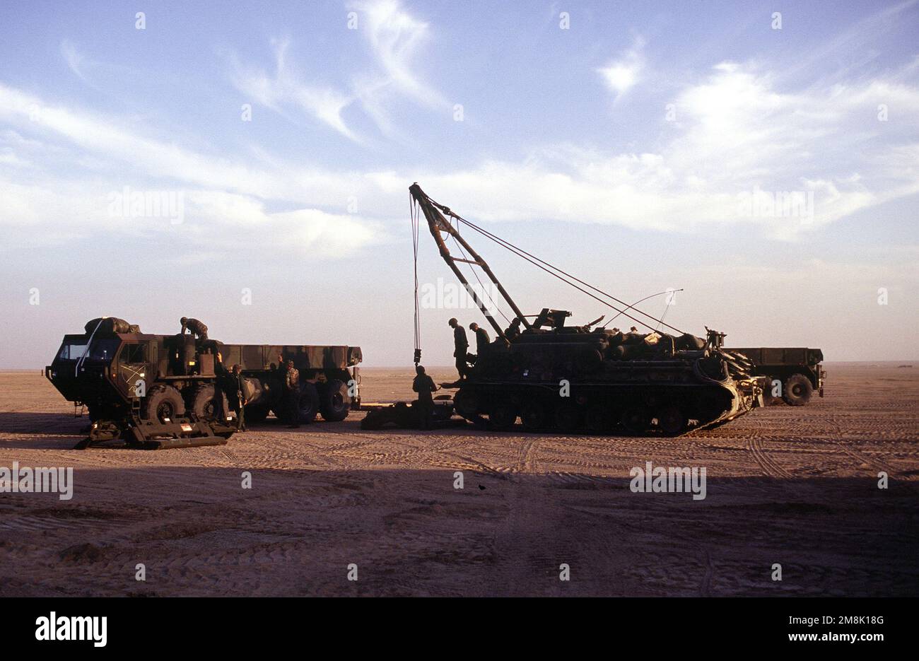 US soldiers use a tank recovery vehicle to load mine plows for the M1A1 ...