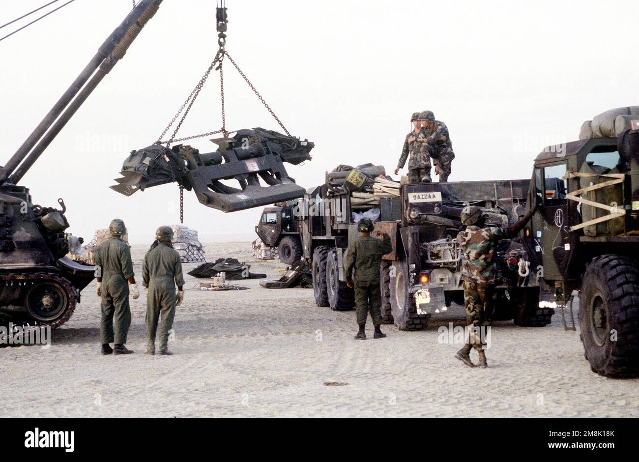 US soldiers use a tank recovery vehicle to load a mine plow for a M1A1 ...