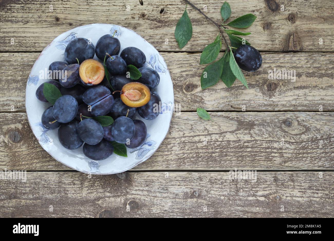 Fresh blue plums in bowl on wooden table background with leaves and ...