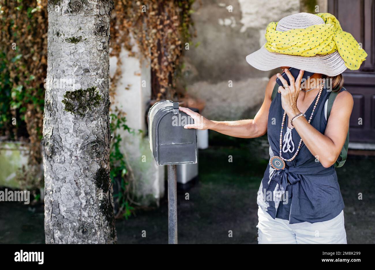 a middle-aged woman wearing a hat check the mailbox at her home ...