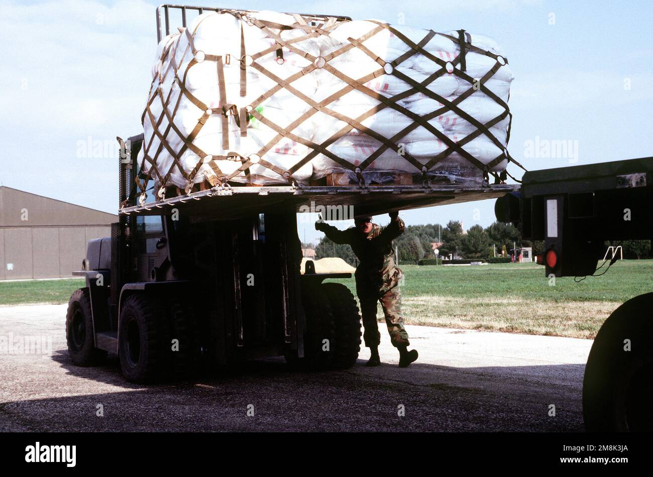 An airman directs a K-loader with a pallet of flour as it backs up the ...