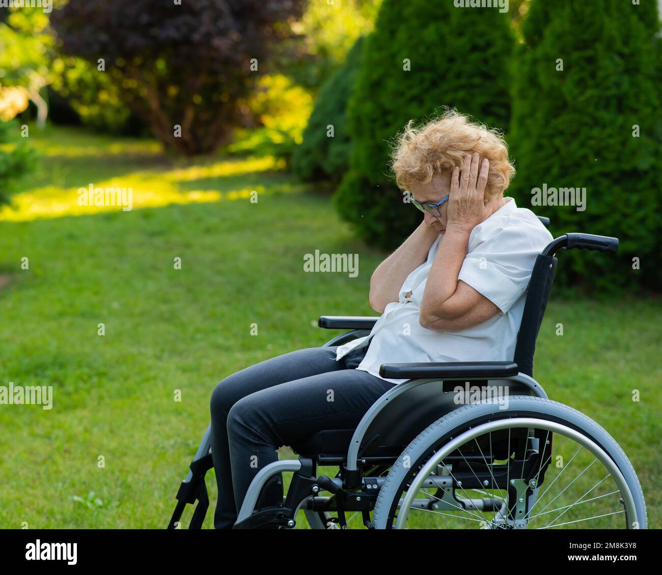 Unhappy elderly woman crying while sitting in a wheelchair on a walk ...
