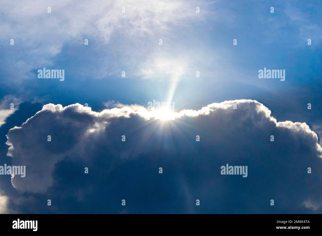 The sun comes out from behind the clouds with blue sky background in ...