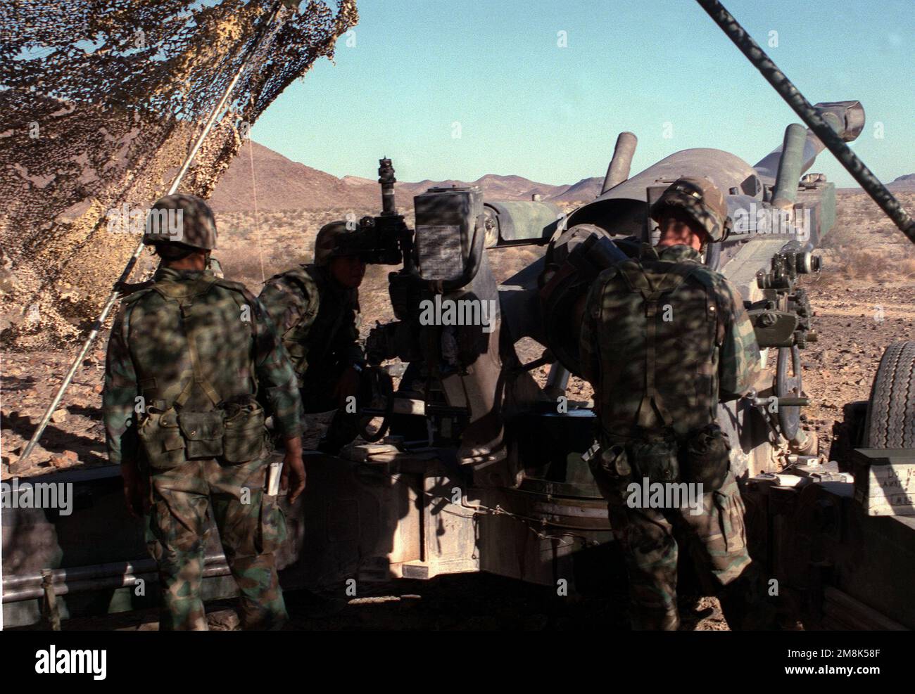 Three gun crewmen, one looking through the M138 elbow telescope, stand ...