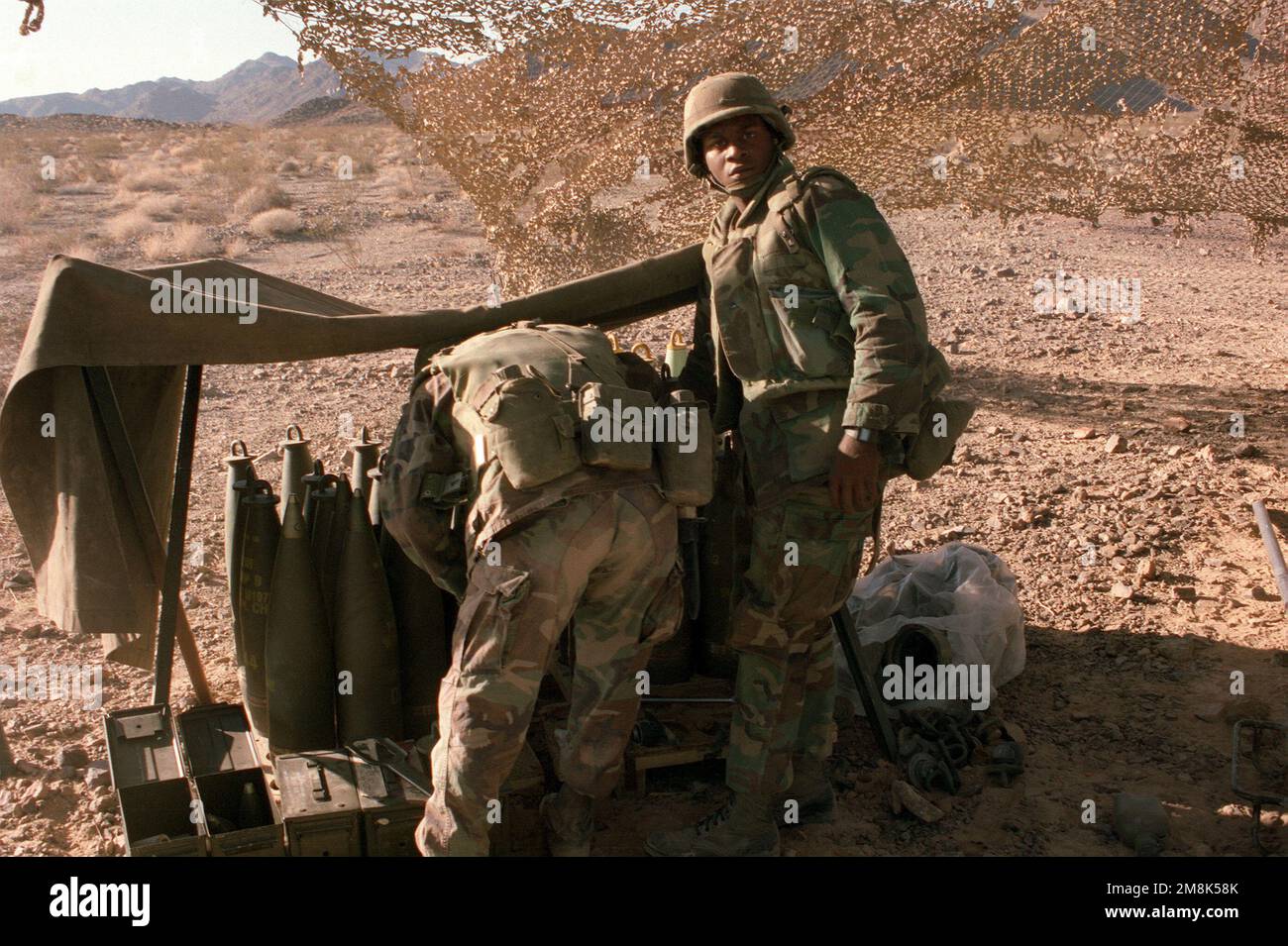 Two gun crewmen in front of a stand of 155 mm projectiles, including ...