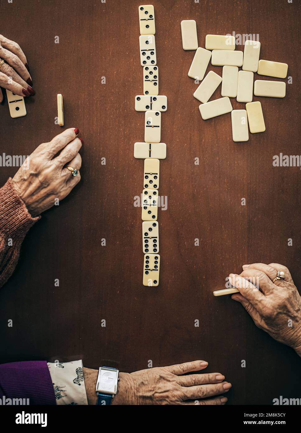 top view of two elderly people playing dominoes on a wooden table ...