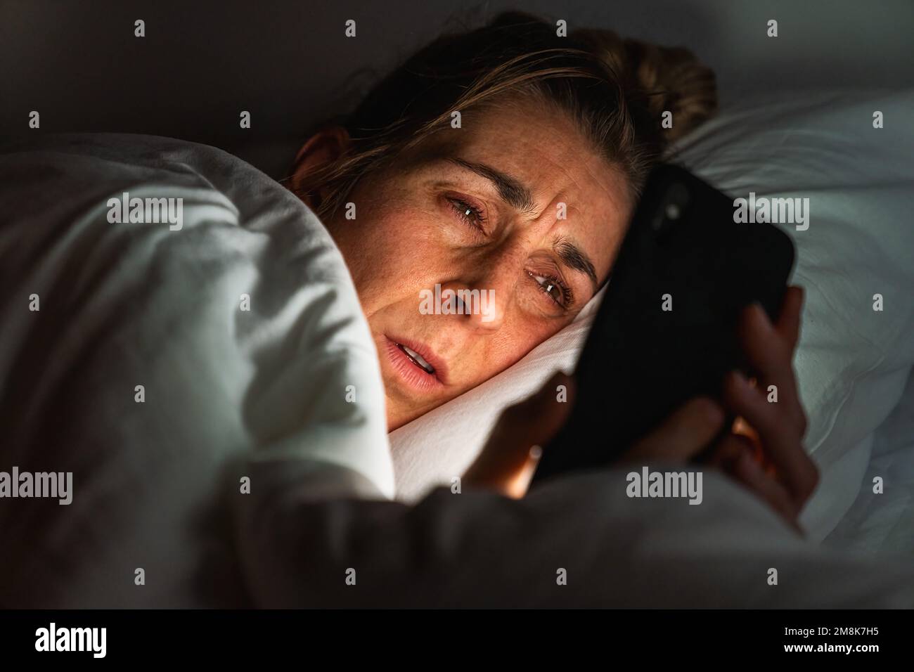 Young woman uses smartphone while lying in bed at night. Insomnia and ...