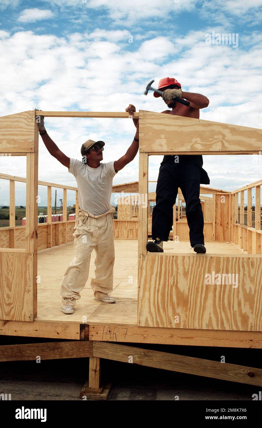 A Cuban migrant carpenter hammers in the nails as another migrant holds ...