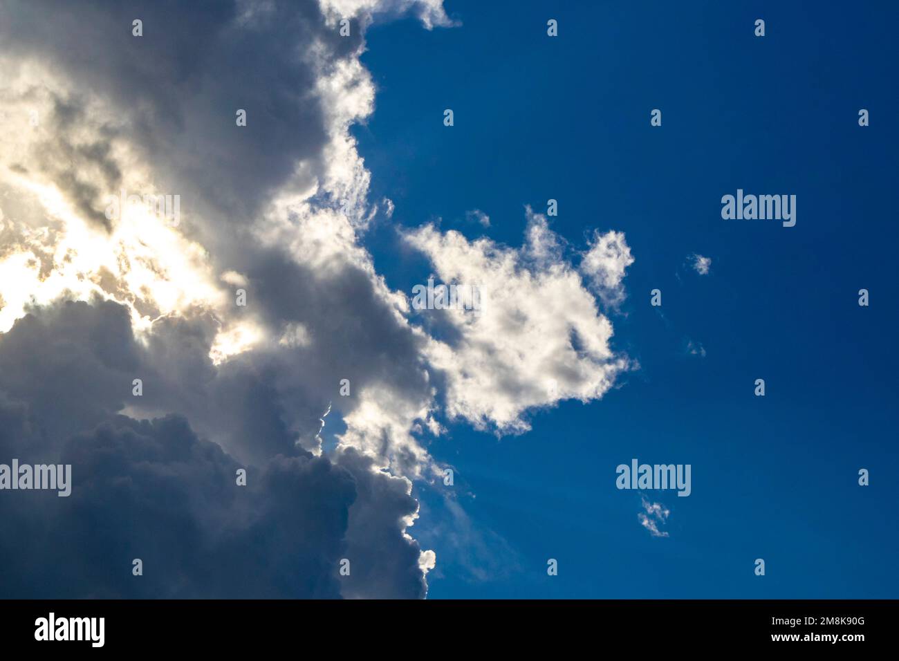 The sun comes out from behind the clouds with blue sky background in ...
