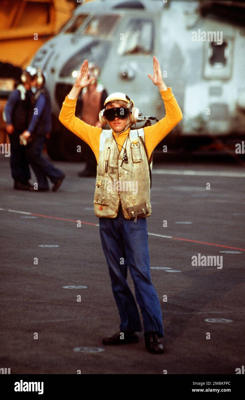 A flight deck crewman signals directions to aircraft as the ship ...