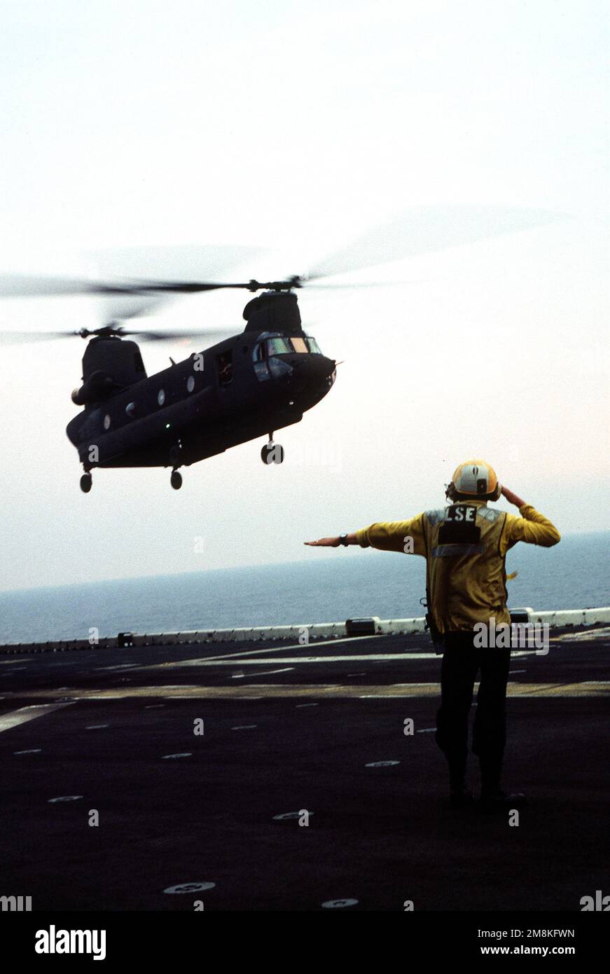 A flight deck crewman on the directs an US Army CH-47D Chinook ...