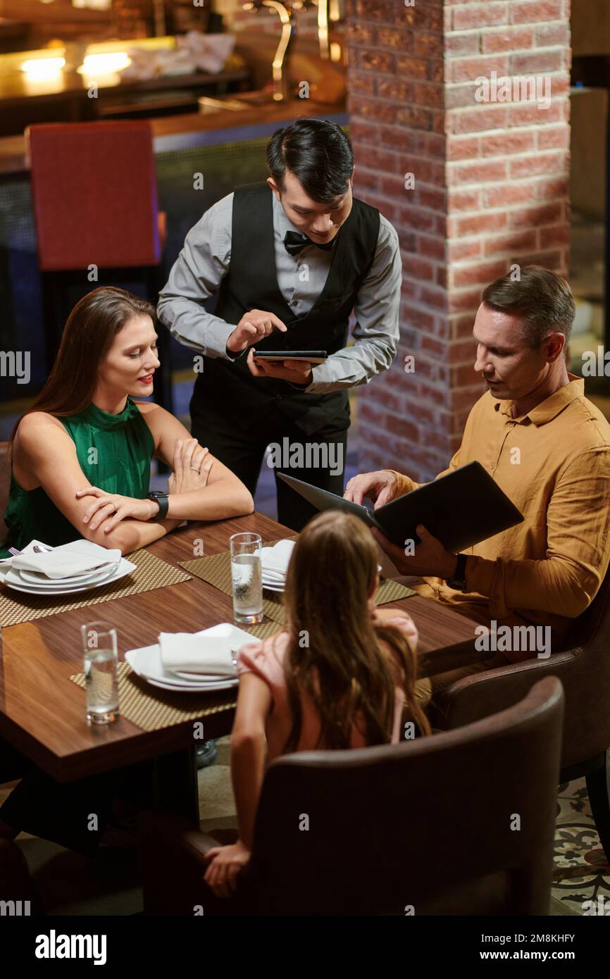 Restaurant waiter taking notes on tablet computer when taking order ...