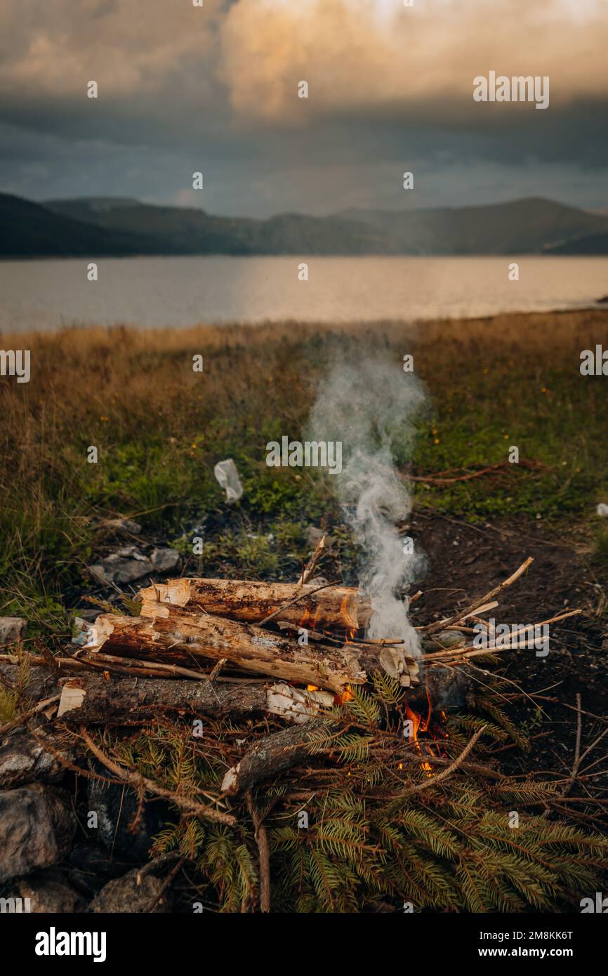 A small campfire with gentle flames beside a lake during a glowing ...