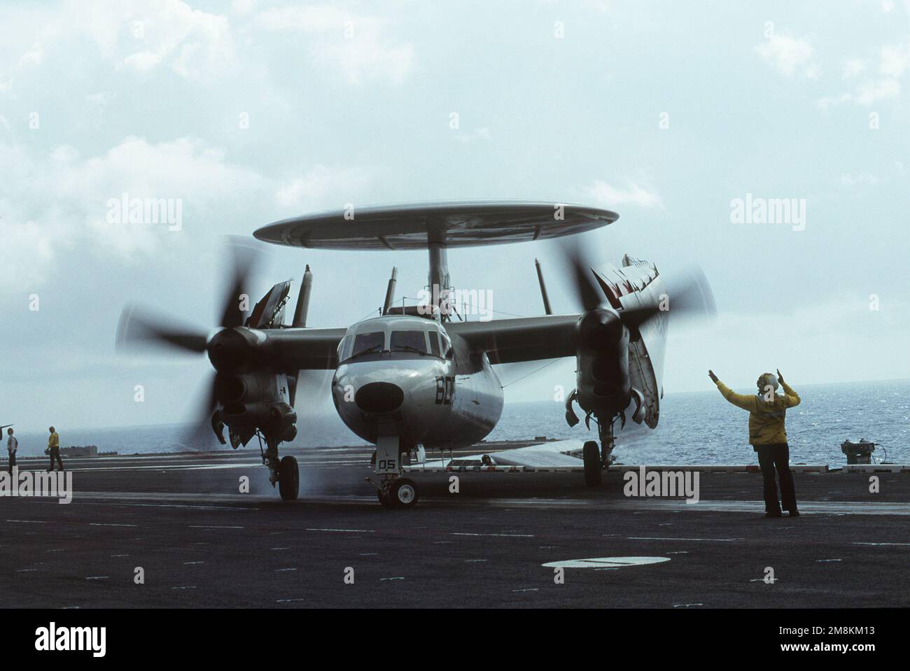 A flight deck crewman signals to the pilot of an E-2C Hawkeye aircraft ...