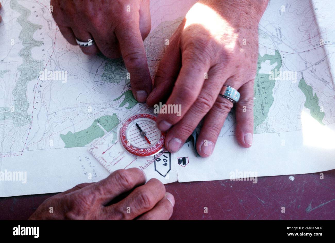 A close up of two pairs of hands using a map and compass as tools for ...