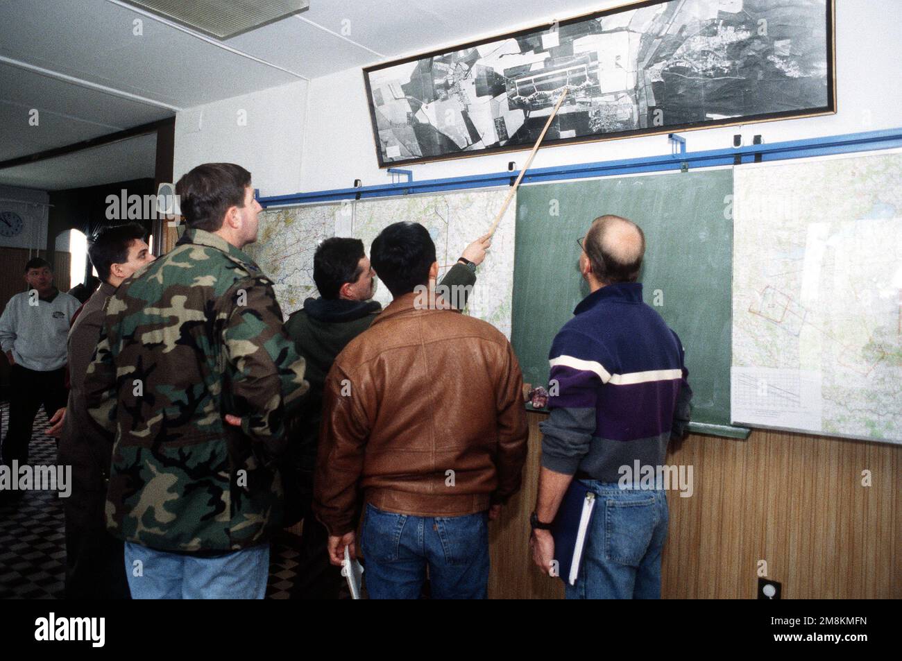 Airfield survey team members are briefed by a Hungarian officer at Taszar, using an aerial map ...