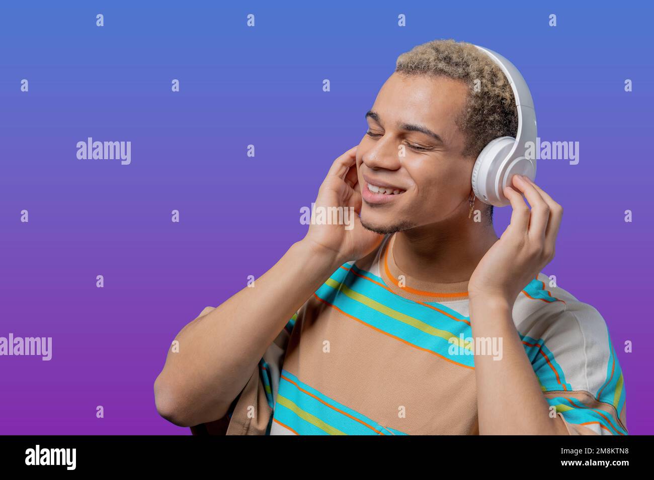 Handsome man listening music, enjoying dance with headphones on violet ...