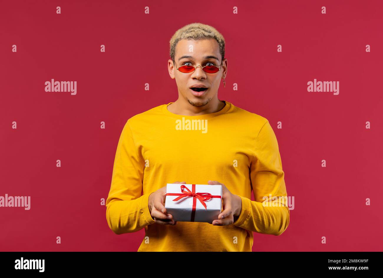 Handsome stylish man with gift box on red background. Guy smiling, he ...