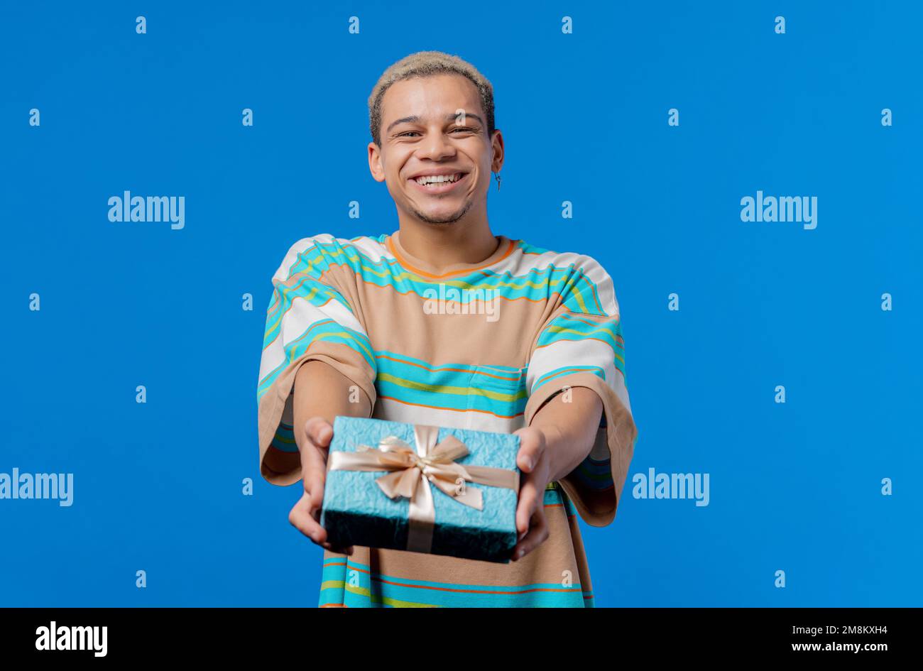 Man gives gift box by hands to camera on blue background. Guy smiling ...