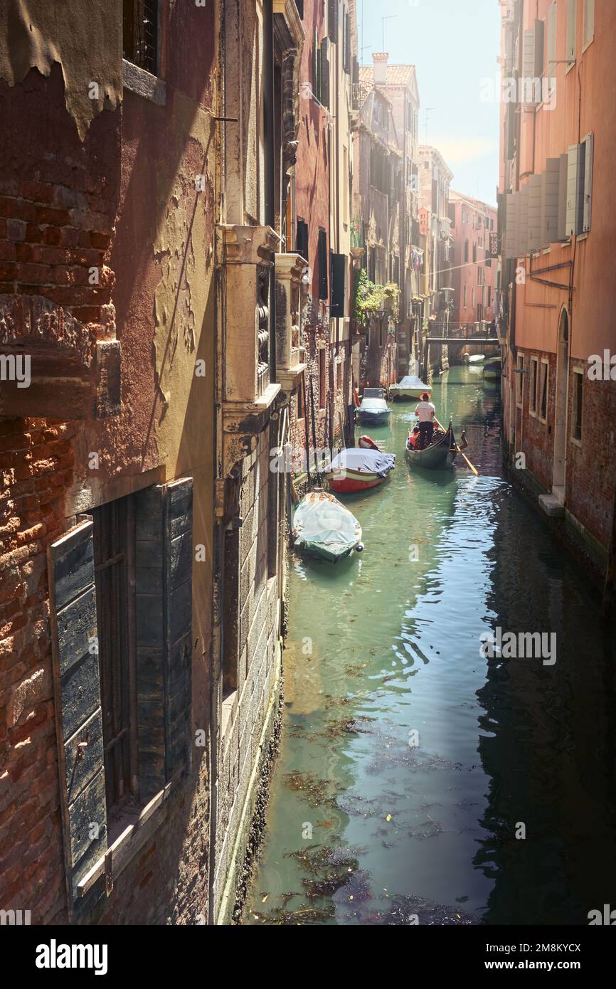View of narrow canal in Venice with gondolier giving people a gondola ...