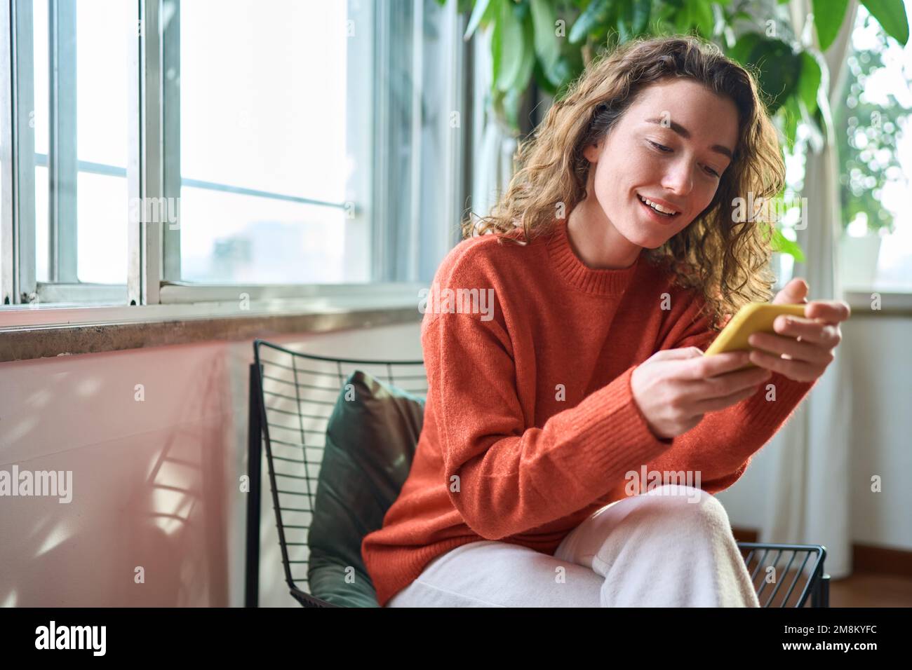 Smiling young woman sitting on chair holding mobile phone using cell at ...