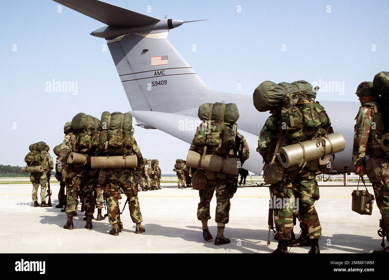 U.S. Army personnel, with field gear and back packs strapped on, wait ...