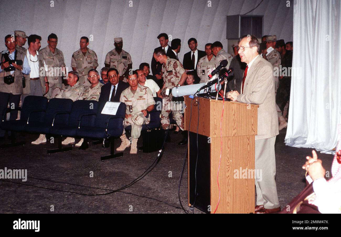 In a hangar, at the podium and with other VIPs seated behind him ...