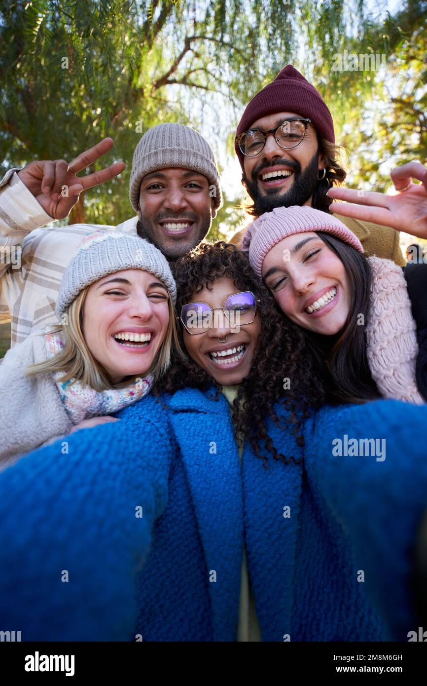 Vertical. Winter time smiling selfie of a happy group of multicultural friends looking at the ...