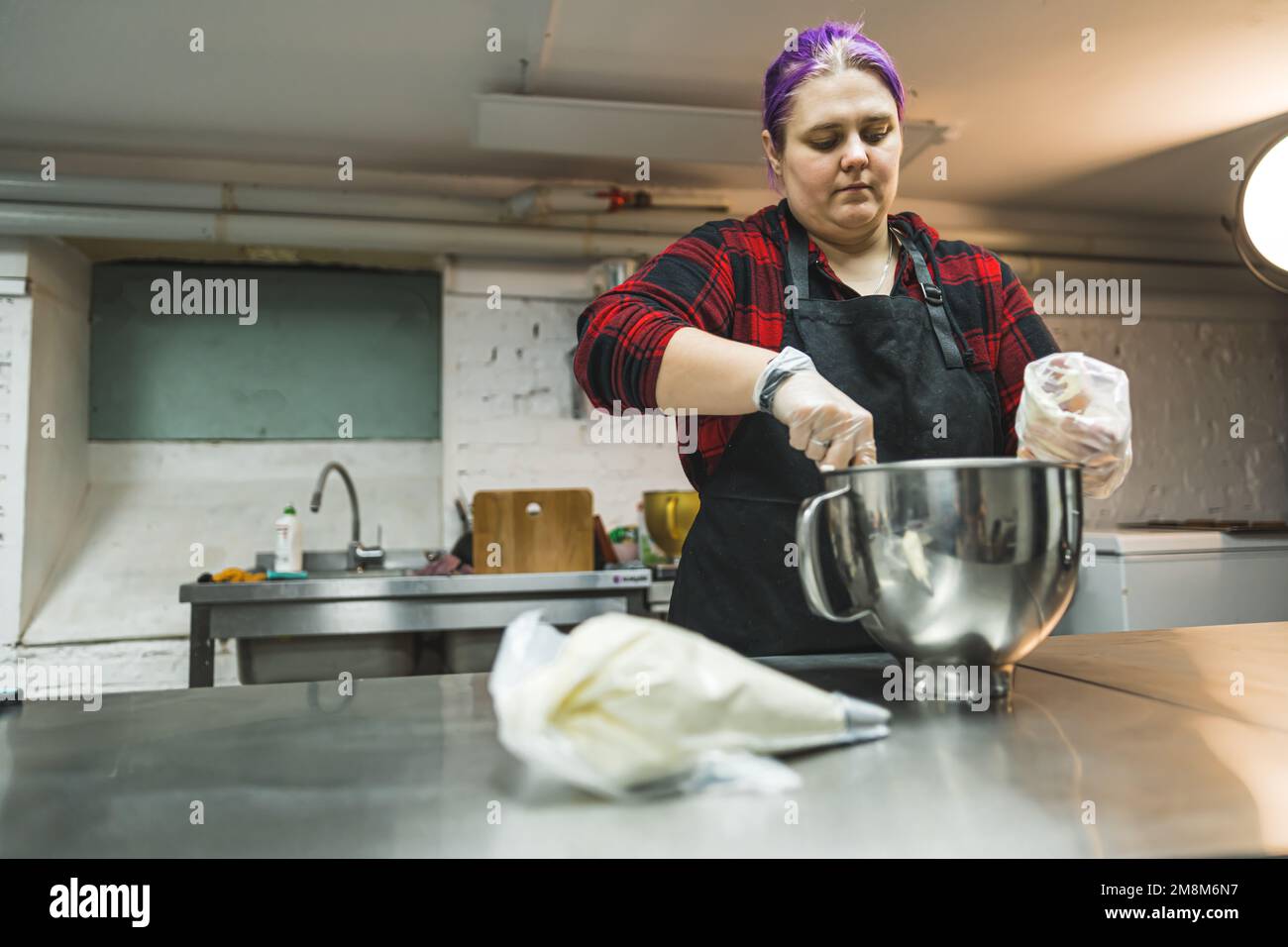 medium shot of a female baker working in the kitchen and glazing in an icing bag in front of her ...
